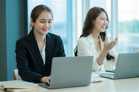 두 명의 아시아 여성 회계사가 노트북 컴퓨터와 금융 문서를 테이블에 올려 놓고 사무실에서 일합니다 2명에 대한 스톡 사진 및