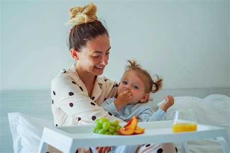 Mãe e filha tomando café da manhã na cama com frutas de pijama conceito de família Foto Premium