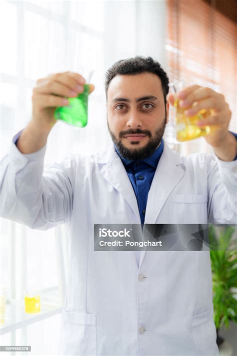 플라스크를 들고 있는 실험복을 입은 백인 과학자 남자는 실험실에서 녹색과 노란색 용액을 들고 있다 실험을 하기 위하여 학생을