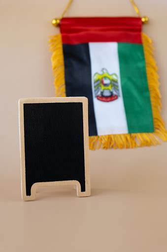 빈 칠판 샘플 화려한 봉투와 함께 베이지 색 배경에 아랍 에미리트 연방의 작은 깃발 공간을 복사합니다 모형 광고 템플릿 아랍 에미리트 국가 상징이 있는 관광 여행 바우처