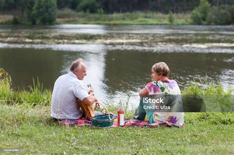 여름날 호수 해안에서 피크닉을 즐기는 동안 아내를 위해 기타를 연주하는 선배 숙박 하이퍼 로컬 여행 가족 나들이 휴양지 기타 현악기에 대한 스톡 사진 및 기타 이미지