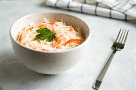 흰색 세라믹 그릇에 수제 소금에 절인 양배추 근처에는 금속 포크와 수건이 있습니다 요리는 파슬리 잎으로 장식되어 있습니다 맛있는 간식 발효 식품 흰색 배경에 밀착되는 컴