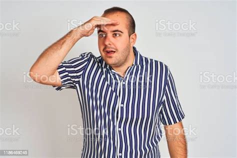 고립 된 흰색 배경 위에 서있는 파란색 줄무늬 셔츠를 입은 청년은 매우 행복하고 머리 위로 손으로 멀리 보고 미소 개념 검색 거리가 먼에 대한 스톡 사진 및 기타 이미지