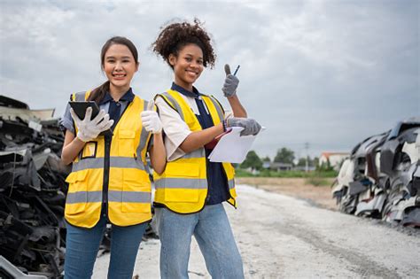 자동차 폐차장에 서서 검사하는 기계 여성 소유자 중소기업 자동차 폐차장에서 예비 부품을 선택하는 더러운 남성 수리공 스크랩 야드