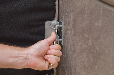 젊은 남자는 렌치와 침대 의 구석에 금속 강철 각도 커넥터에 나사를 사용하여 손 소파의 일부를 함께 넣어 새로운 섬유 가구를 조립 근접 촬영 Diy에 대한 스톡 사진 및