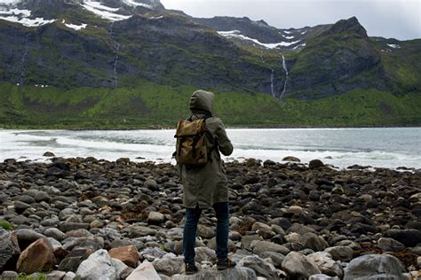 빈 바다 해변을 따라 걷고 산을 바라보는 배낭을 가진 남자 노르웨이의 피요르드 경치 여행 모험 자유의 감각 라이프 스타일 로포텐 제도 노르웨이 노스 서머 걷기에 대한 스톡