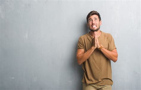 구걸 하 고 손으로 얼굴 매우 감정적이 고 걱정에 희망 식 함께 기도 회색 그런 지 벽에 잘생긴 젊은 남자 용 서에 대 한 요구 종교 개념입니다 감정에 대한 스톡 사진 및