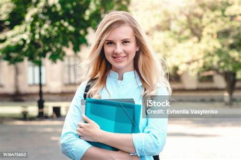 금발의 한 학생 소녀가 웃으며 대학 배경에서 폴더와 노트북을 손에 들고 있습니다 한 소녀가 공원 배경에 서 있습니다 30 34