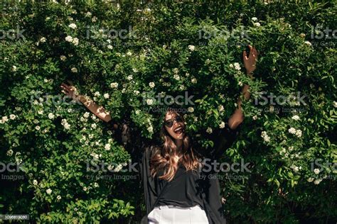 화창한 날에 꽃 덤 불에서 편안한 아름 다운 머리를 가진 아름 다운 세련 된 Hipster 소녀 꽃 정원에서 하루를 즐기고 유행 복장에 선글라스와 함께 행복 한 Boho