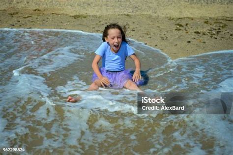 보라색 드레스에 화창한 날에는 해변에 노란 모래에 앉아 재생 및 그녀는 웨이브 롤 때 쾌활 한 작은 소녀 가로 방향 귀여운에 대한 스톡 사진 및 기타 이미지 Istock