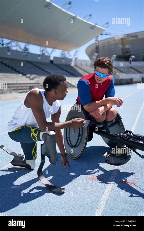 Male Amputee And Wheelchair Athletes Talking On Sunny Sports Track