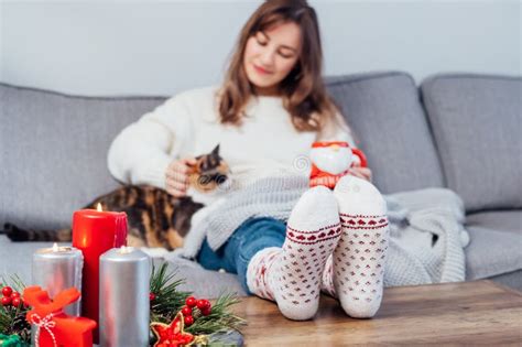 Focus On Feet In Xmas Woolen Socks With Blurred Woman With Festive Cup Petting Cat On Sofa At
