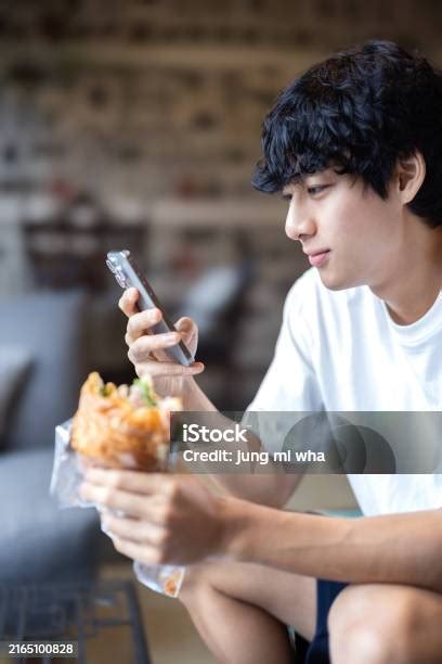 낮에는 한 청년이 카페에서 의자에 앉아 스마트폰으로 휴식을 취하고 있습니다 20 24세에 대한 스톡 사진 및 기타 이미지 20 24세 Brand Name Smart