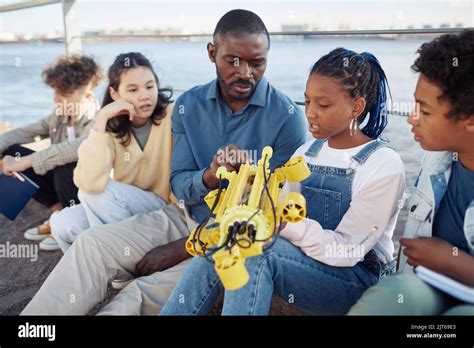 Portrait Of Young Black Girl Holding Robot Model During Engineering Class Outdoors With Male