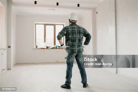 단단한 모자를 쓴 빌더 수리공은 빈 방에 등을 대고 서 있습니다 가사 집안일에 대한 스톡 사진 및 기타 이미지 가사 집안일 건설 산업 건설 장비 Istock