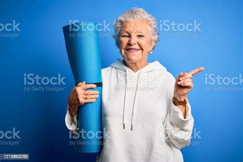 시니어 아름다운 스포티 한 여자 들고 매트 용 요가 서 위에 고립 된 파란색 배경 매우 행복 가리키는 손과 손가락 으로 측면에 가리키기에 대한 스톡 사진 및 기타 이미지