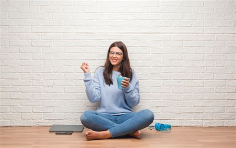 젊은 갈색 머리 여자 백색 벽돌 벽 마시는 커피 자랑 비명과 승리와 성공을 매우 흥분된을 축 하 하 고 바닥에 앉아 감정을 응원