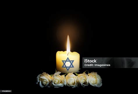 이스라엘 국기와 함께 어두운 배경에 불타는 촛불이 있는 하얀 장미 장례식 꽃과 촛불은 검은 배경에 테이블에 있다 장례식 상징 기분과 애도 카드 개념 장례식에 대한 스톡 사진