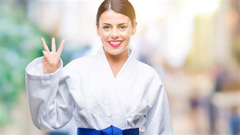 젊은 아름 다운 여자에가 라 데 기모노 유니폼을 입고 절연 배경 표시 하 고 자신감과 행복 미소 하는 동안 3 번 손가락으로 가리키는 가라테에 대한 스톡 사진 및 기타