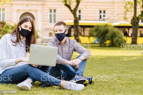 풀밭 에서 밖에서 공부하는 얼굴 가면을 쓴 유럽 학생 부부는 노트북 컴퓨터를 사용하여 학교 캠퍼스에 앉아 여름 햇살 아래에서 나무 자연 아래에서 열심히 공부합니다 캠퍼스에