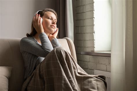 헤드폰을 쓰고 소파에 앉아 담요에 앉아 컵을 마시고 창문을 보고 음악을 듣는 Aucasian 젊은 여성의 초상화 가리기에 대한 스톡 사진 및 기타 이미지 Istock