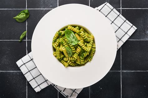 페스토와 이탈리아 푸실리 파스타 검은 돌 조리대 배경에 바질 페스토와 허브 파르 메산 치즈 바질 및 마늘을 흰색 접시에 곁들인 Fusilli 파스타 상단 보기 공간을