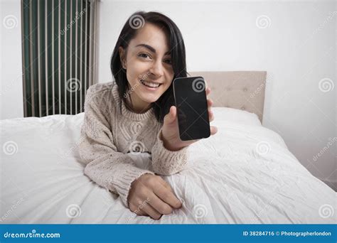Портрет счастливой женщины показывая умный телефон пока лежащ в кровати Стоковое Фото