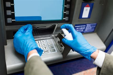 Atm 기계를 소독하기 위해 알코올 스프레이를 사용하는 여성 보호 마스크와 장갑을 가진 여자는 도시 거리에 서서 현금을 인출하기 위해 Atm 기계를 사용 코로나 또는