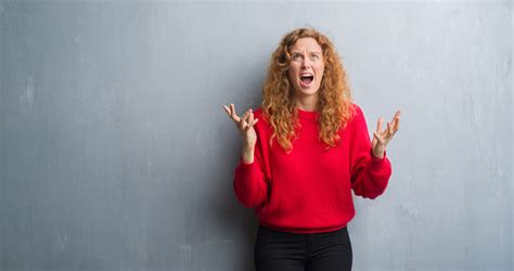 빨간 스웨터 미친과 미친 소리 하 고 적극적인 식와 팔 제기 함 입고 회색 그런 지 벽에 빨강 머리 젊은 여자 좌절 개념입니다 감정에 대한 스톡 사진 및 기타 이미지