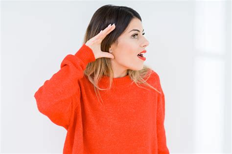 젊은 여성 고립 된 배경 위에 캐주얼 빨간 스웨터를 착용 귀 위에 손으로 웃 고 소문 또는가 십에 청각을 듣고 청각 장애 개념 귀 부분에 대한 스톡 사진 및 기타 이미지