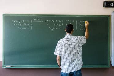 Math Teacher Writing Formulas On Chalkboard In Classroom Stock Photo