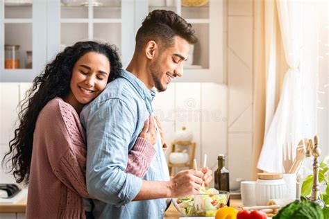 Loving Arab Woman Hugging Husband From Back While He Cooking In Kitchen