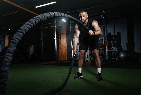 보디 빌더는 체육관 홀에서 근육 피트니스를위한 배틀 로프와 종사하고 있습니다 근력을 위한 격렬한 운동으로 훈련과 지구력 텍스트를 위한 공간 35 39세에 대한 스톡 사진 및