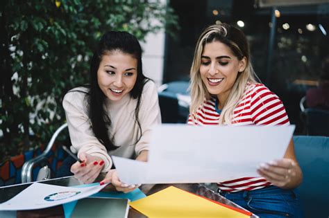 보도 카페에서 공동 공부하는 동안 종이 문서를 분석하는 쾌활한 다인종 여성 친구 연구에 유익한 보고서를 사용하여 대학 숙제를하는