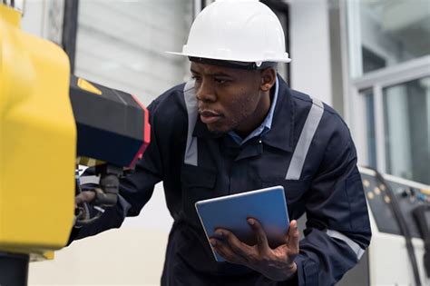 자동 로봇 팔을 확인하거나 유지 관리하기 위해 태블릿을 사용하는 아프리카계 미국인 남성 엔지니어 또는 전기 기술자 남성 기술자 작업자 검사 수리 자동 로봇 30 34세에