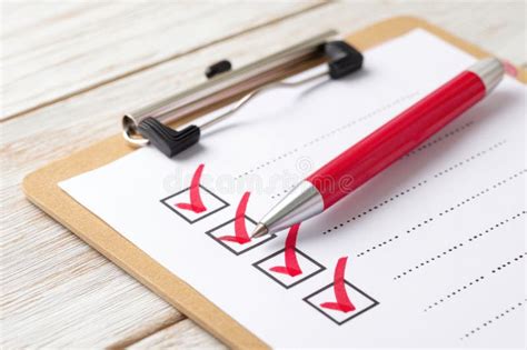 red pen checking boxes on checklist on clipboard on wooden table stock