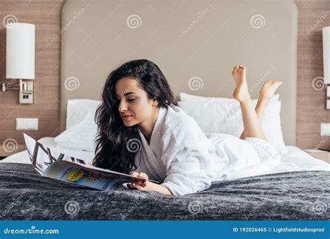 Barefoot Brunette Young Woman In White Bathrobe Lying On Bed And