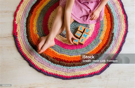 4 살 어린 아이는 흰색 라미네이트 바닥에 용도가 변경 된 티셔츠 원사에서 둥근 다채로운 크로 셰 뜨개질 양탄자에 앉아 편지와 자연 나무 큐브를 재생합니다 위 보기 위입니다