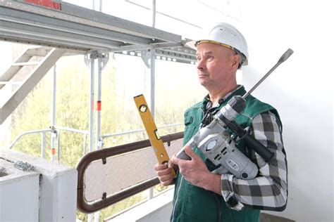 Elderly Builder With A Hand Tool In A Protective White Helmet And
