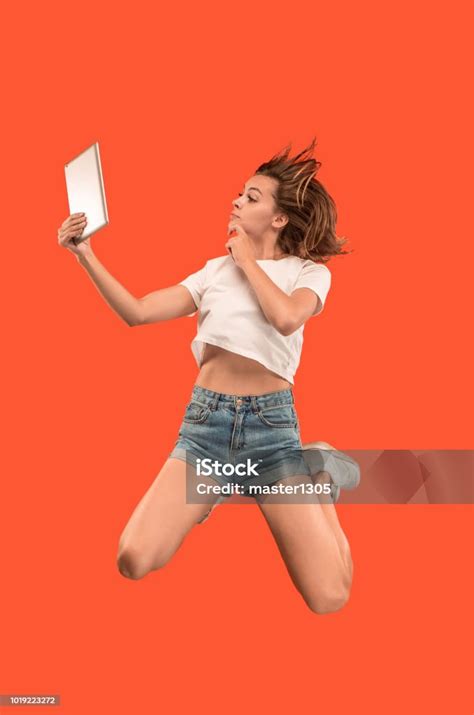 노트북 컴퓨터나 태블릿 가제트를 사용 하 여 점프 하는 동안 빨간색 배경 위에 젊은 여자의 이미지 스튜디오에 대한 스톡 사진 및 기타 이미지 Istock