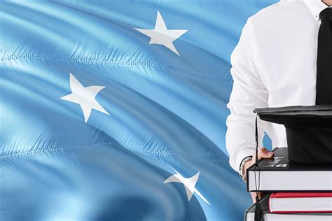 성공적인 마이크로 시안 학생 교육 컨셉 미크로네시아 국기 배경에 책과 졸업 모자를 들고 Micronesian Flag에 대한 스톡 사진 및 기타 이미지