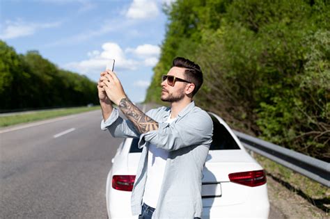 화가 난 청년이 고장난 자동차 옆 도로에 서서 핸드폰으로 손을 들고 길가 도움을 청하려고 애쓴다 긴급 표시에 대한 스톡 사진 및 기타 이미지 Istock