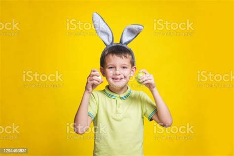 부활절 토끼 귀를 가진 귀여운 어린 소년이 두 개의 다채로운 부활절 달걀을 들고 있습니다 노란 배경에 토끼 귀와 부활절 달걀을 가진 소년 검색에 대한 스톡 사진 및 기타
