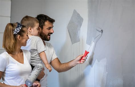 아버지는 한 손에 아이를 안고 다른 손으로 새 아파트의 벽을 칠하고 여자는 옆으로 서서 페인트 롤러를 손에 들고 있습니다 그림 그리기에 대한 스톡 사진 및 기타 이미지