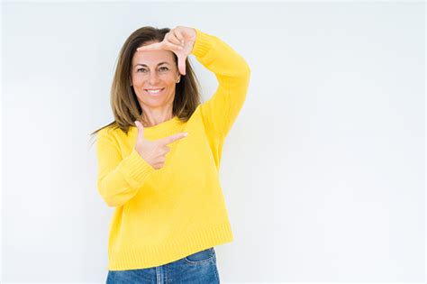 행복한 얼굴로 손과 손가락으로 프레임을 만드는 고립 된 배경 에 노란색 스웨터를 입고 아름다운 중년 여성 창의력과 사진 개념 갈색 머리에 대한 스톡 사진 및 기타 이미지