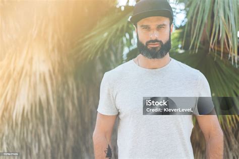 Hipster 캐주얼 도시 스타일에 회색 공백 T셔츠와 귀하의 로고 또는 디자인에 대 한 공간을 가진 검은 Snapback 모자를 착용 하는 수염과 잘생긴 남성 모델 그린