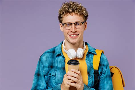 캐주얼 한 옷 배낭 헤드폰 안경을 쓴 젊은 행복한 소년 십대 학생은 보라색 배경 스튜디오에서 고립 된 테이크 아웃 배달 컵 커피를 보유하고 있습니다 고등학교 대학 개념교육