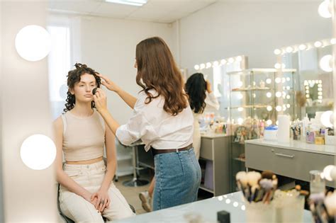 뷰티 스튜디오에서 예쁜 젊은 여성의 얼굴 조각을 위해 화장품 색조 파운데이션을 적용하는 알아볼 수 없는 여성 메이크업 아티스트의