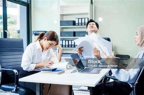 한 무슬림 사업가가 중년으로 보이는 아시아계 남성과 여성과 함께 노트북이 놓인 책상에 앉아 기업 환경에서 어려운 비즈니스 문제를 논의하면서 스트레스를 받는 것처럼 보입니다