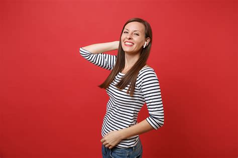 무선 이어폰 밝은 빨간 벽 배경에 고립 된 음악 듣기와 캐주얼 스트라이프 옷에서 웃는 젊은 여자의 초상화 사람들이 진심으 감정